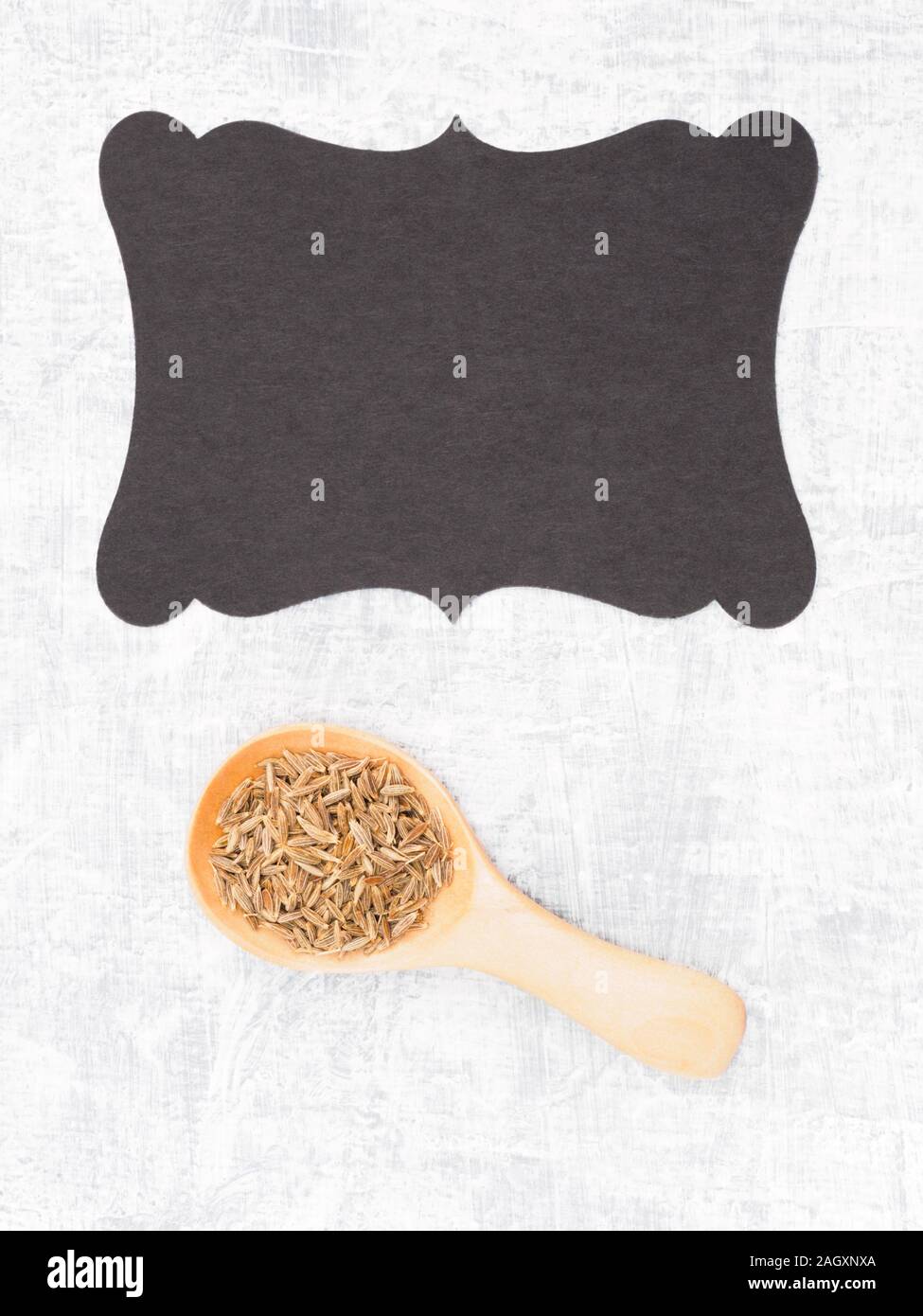 Cumin (jeera) in wooden spoon, nameplate on a white concrete background ...