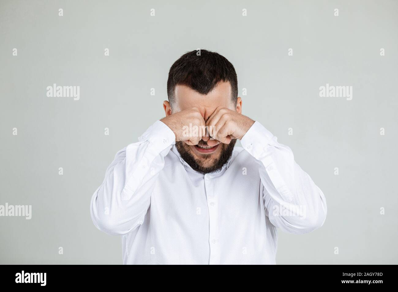 portrait of funny bearded man is crying and wiping tears on gray ...