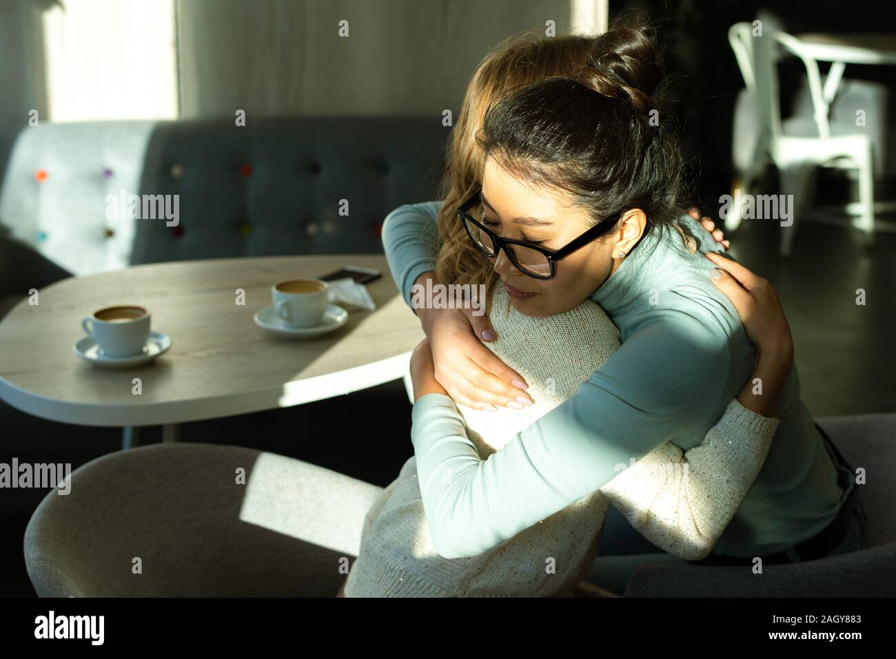 Two young affectionate intercultural women giving hug to each other in ...