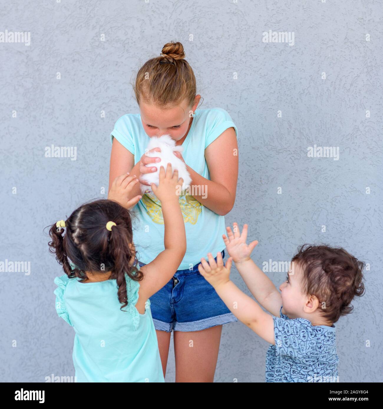 Teenage child holding a cute little white furry rabbit. Three happy ...