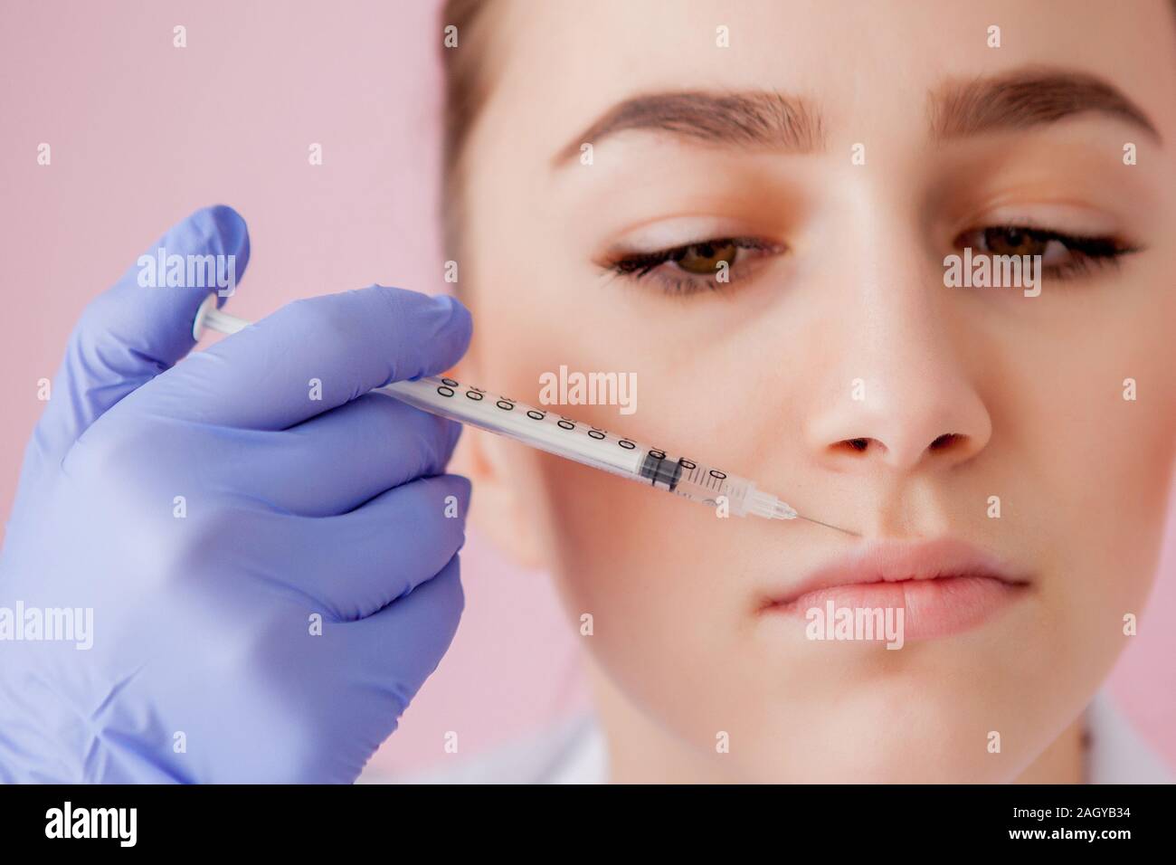 Doctor in gloves giving woman botox injections in lips, on pink ...