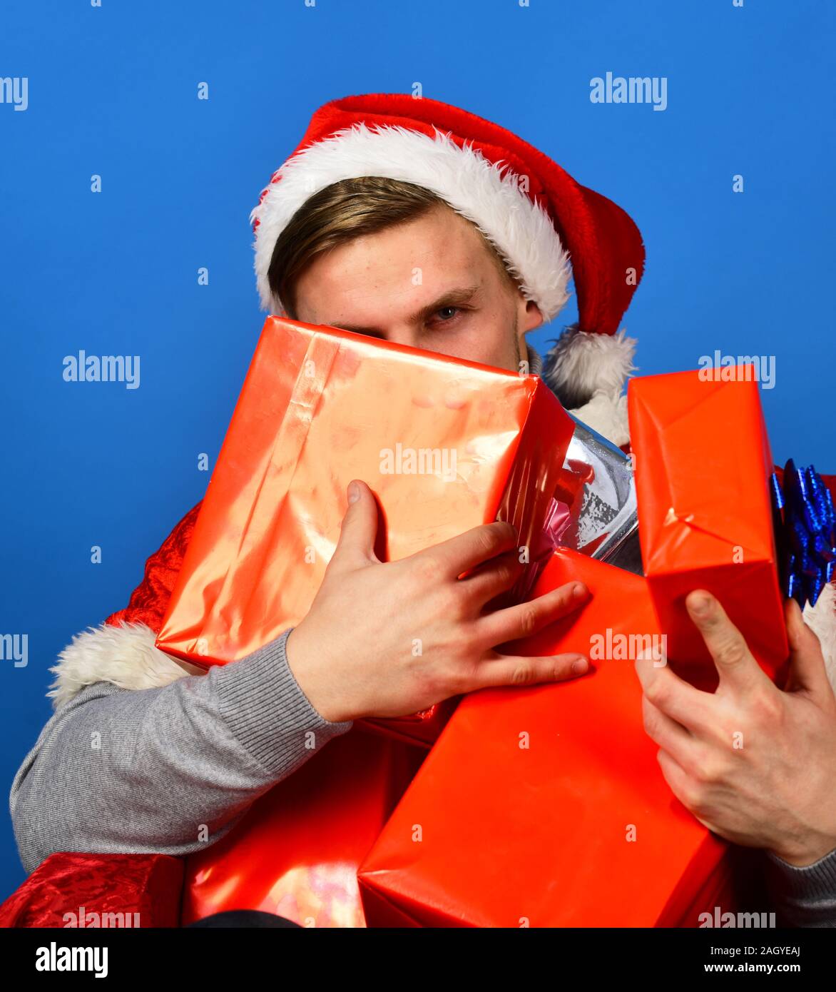 Man hides behind Christmas gifts. Santa with many presents on blue ...