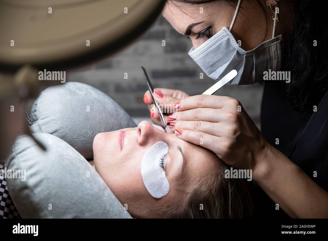 Extensions of artificial eyelash, process close up. Woman in beauty ...