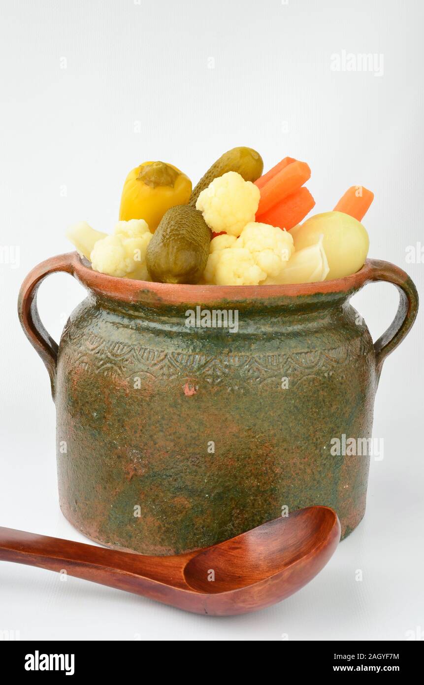 Pickled vegetables in a clay pot with a wooden dipper over white ...