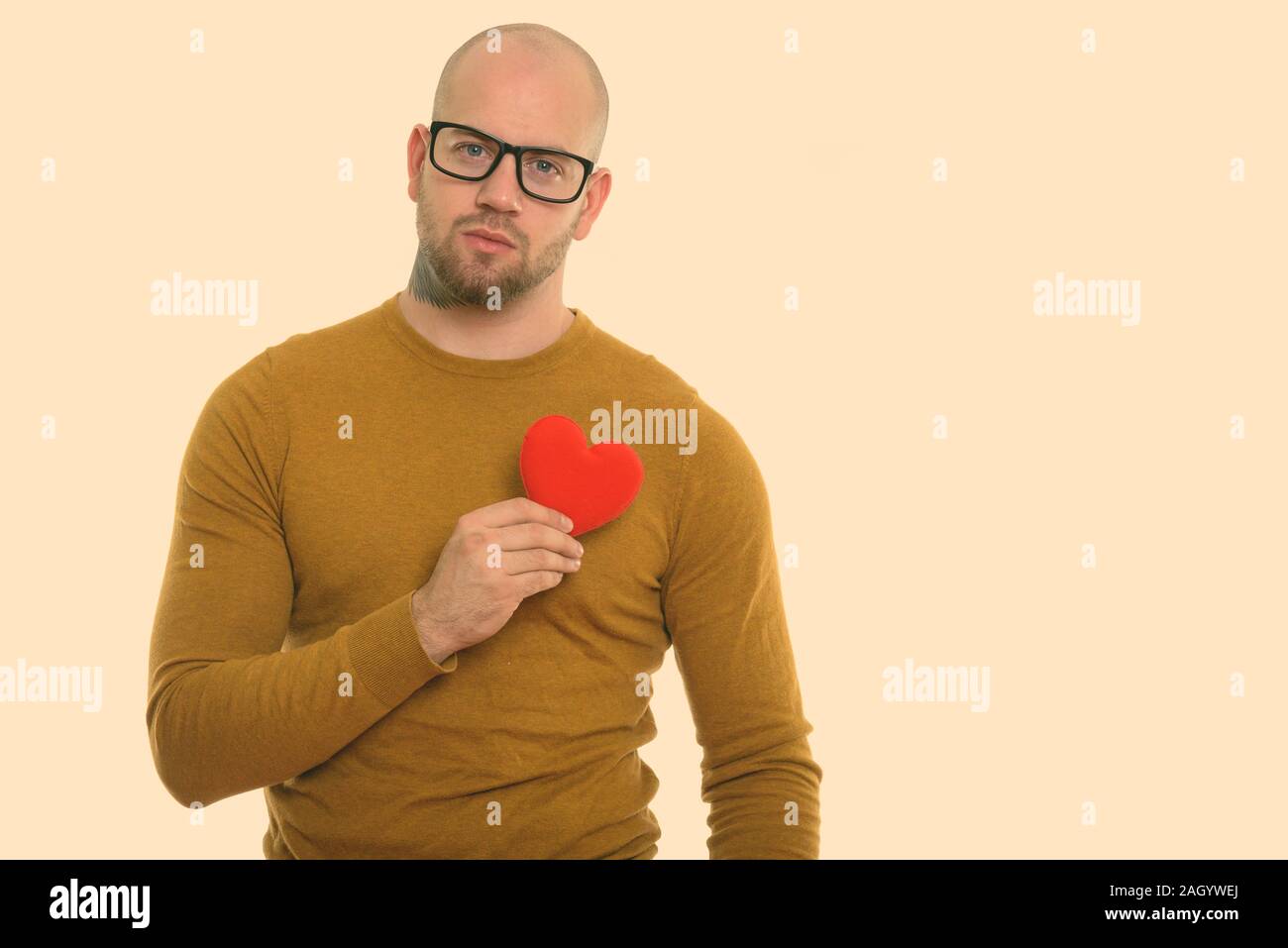 Studio shot of young bald muscular man holding red heart against chest ...