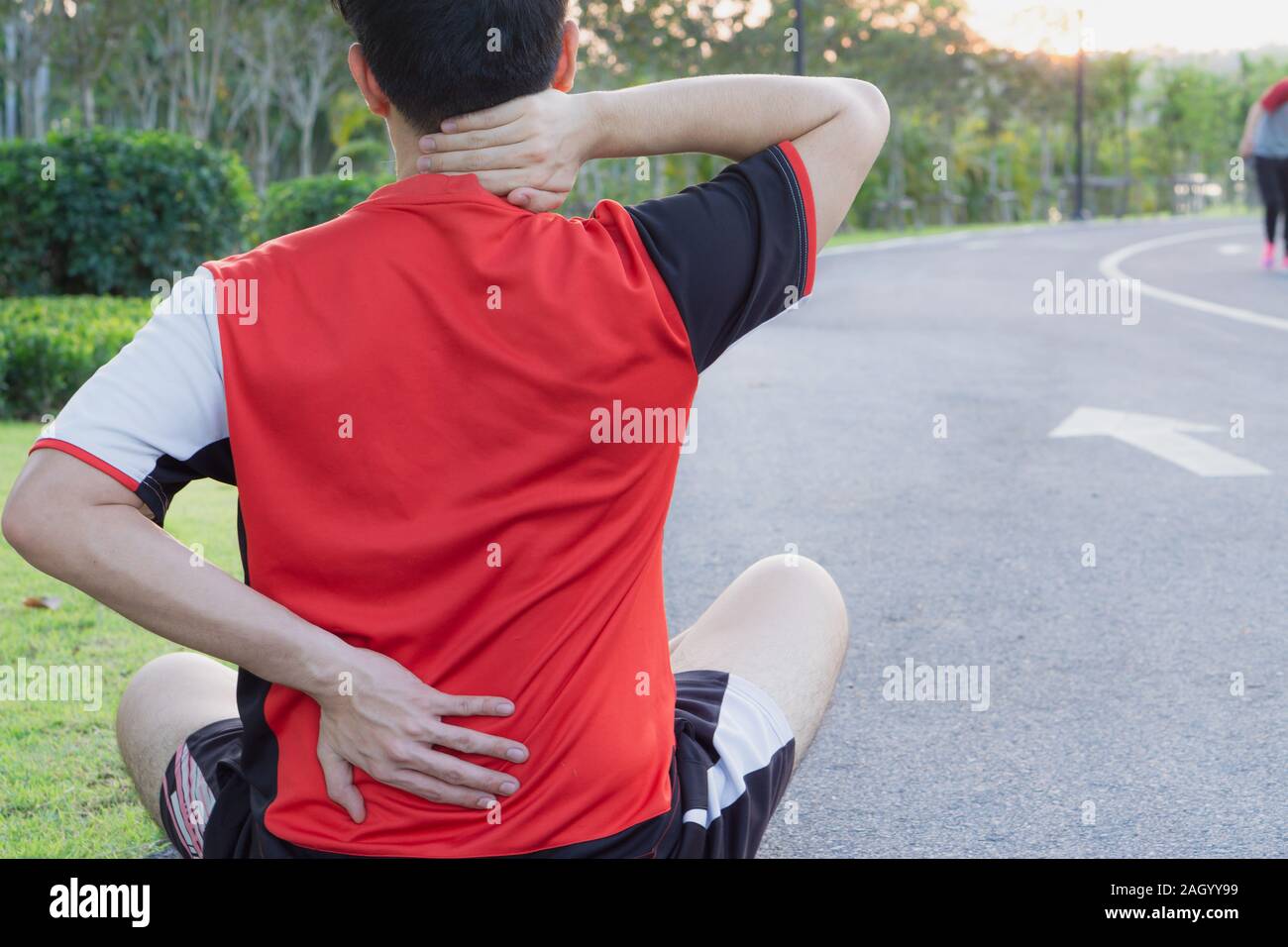 A male athlete suffering from neck and back pain and injury at the park ...