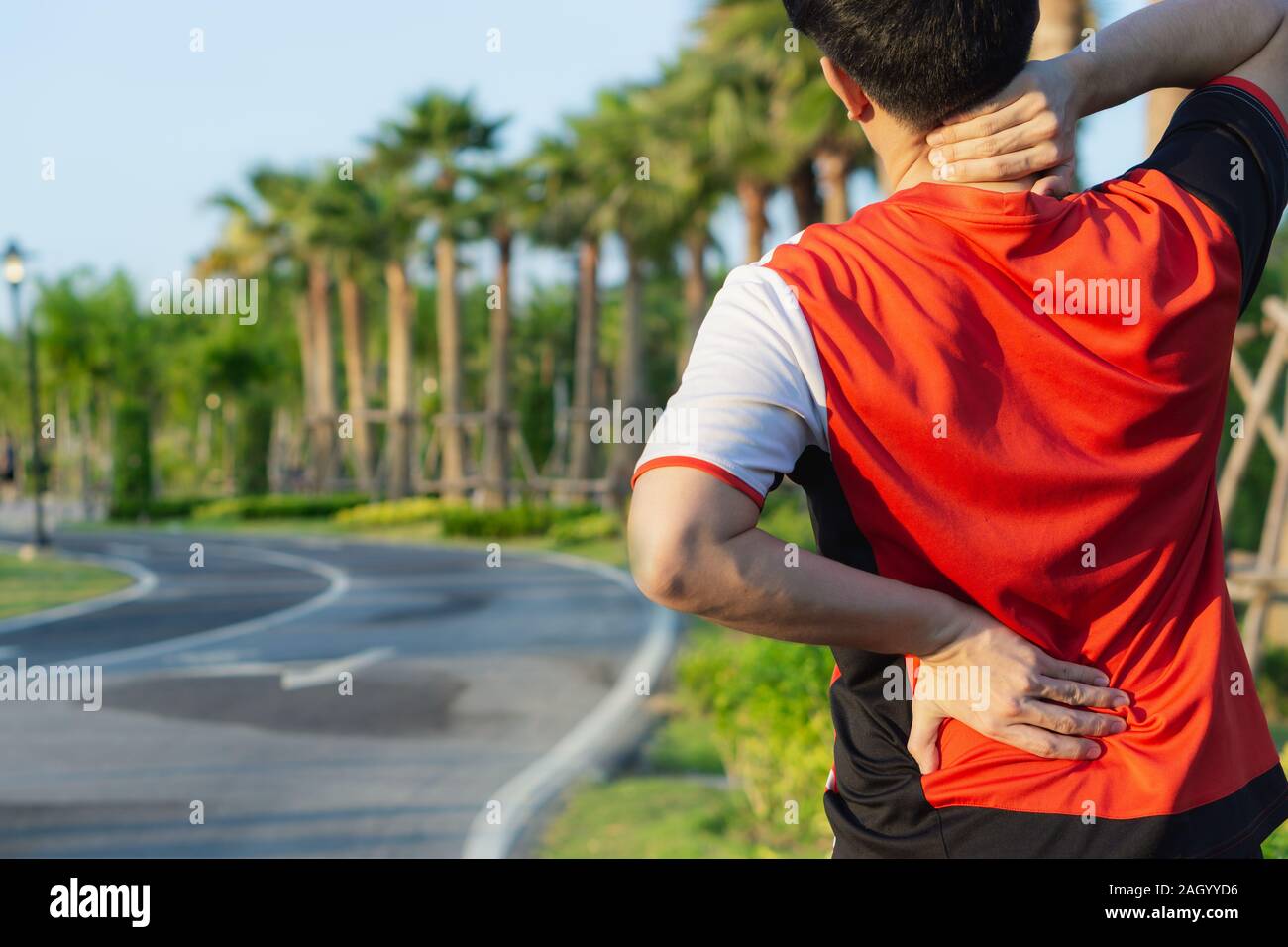 A male athlete suffering from neck and back pain and injury at the park ...