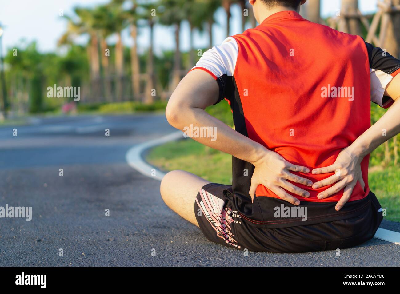A male athlete suffering from neck and back pain and injury at the park ...