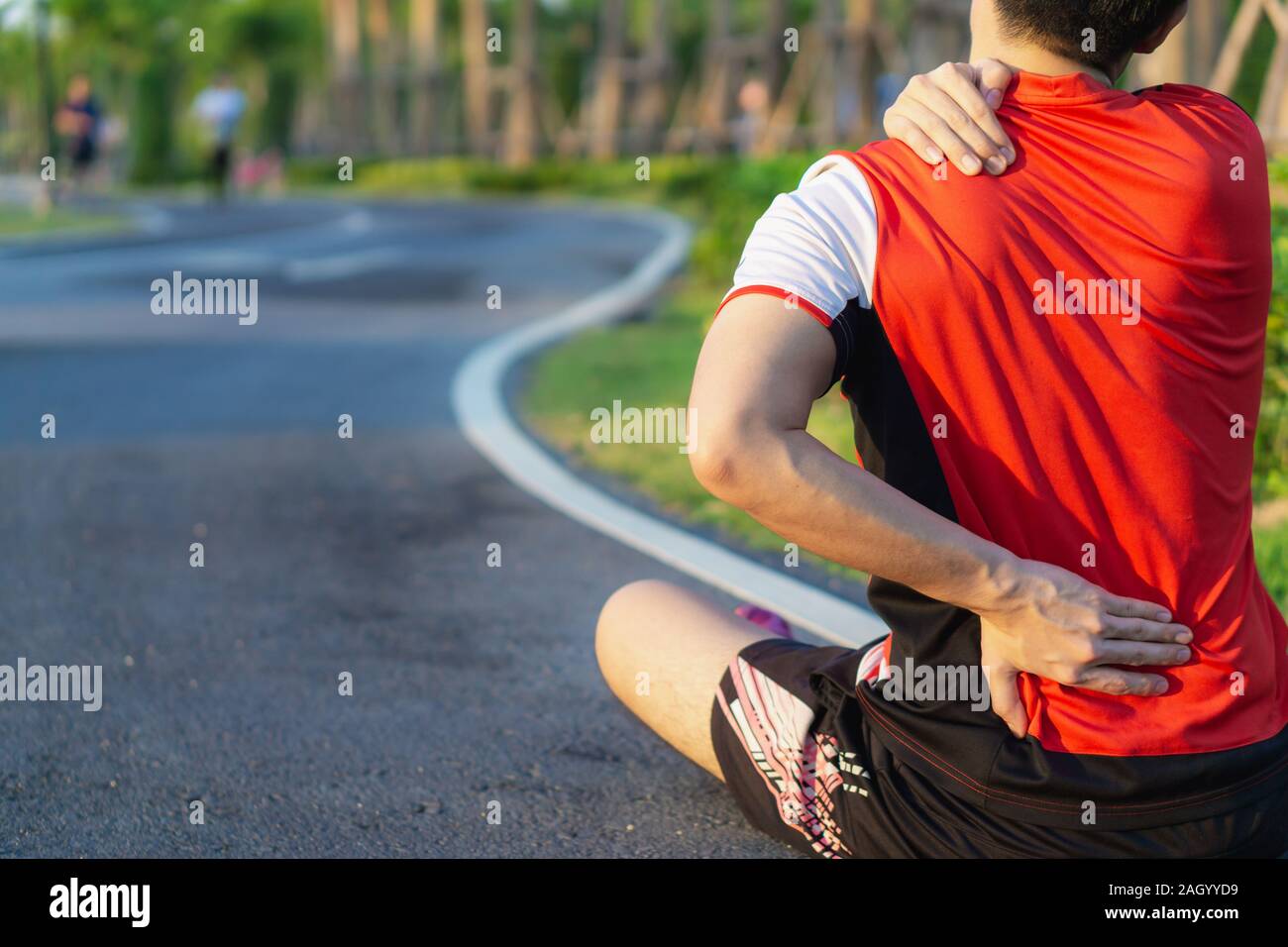 A male athlete suffering from neck and back pain and injury at the park ...