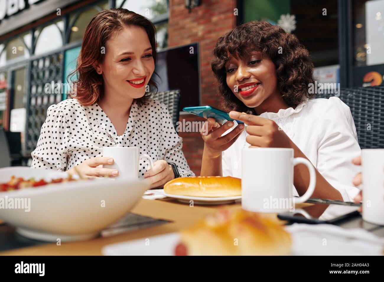 Cheerful multi-ethnic female friends photographing food when having ...