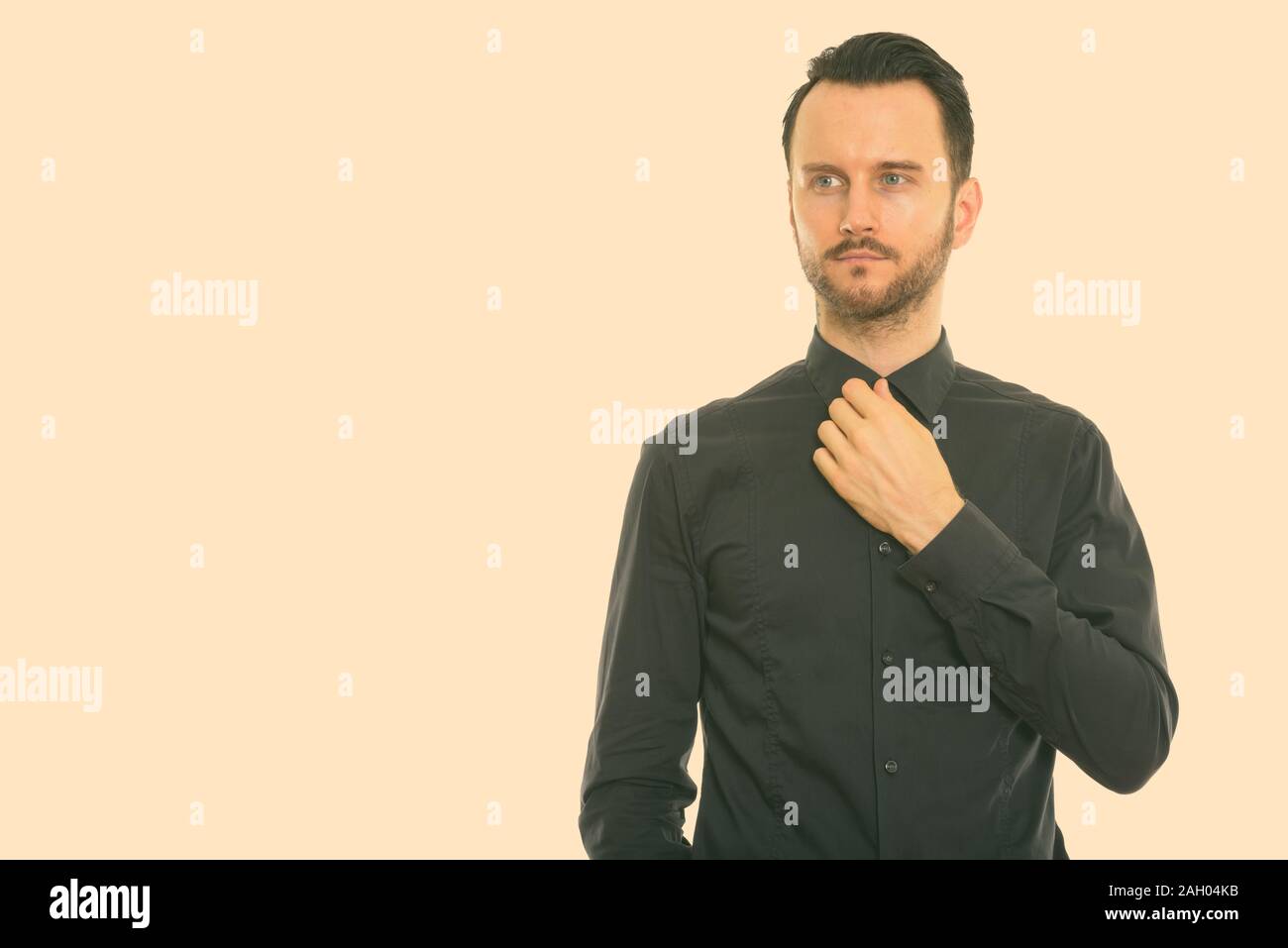 Studio shot of young man thinking while fixing his collar Stock Photo ...