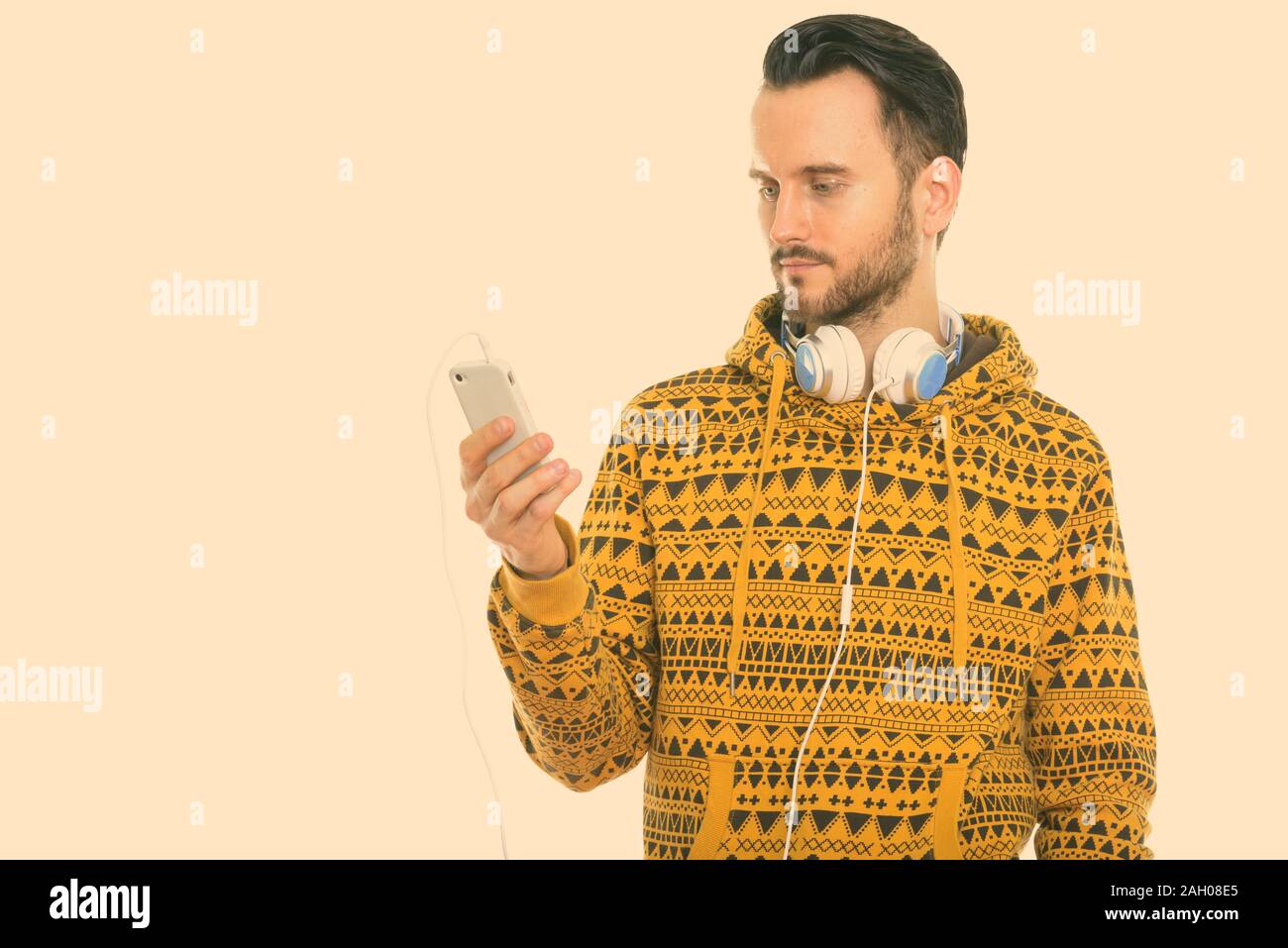 Studio shot of young man using mobile phone while wearing headphones ...