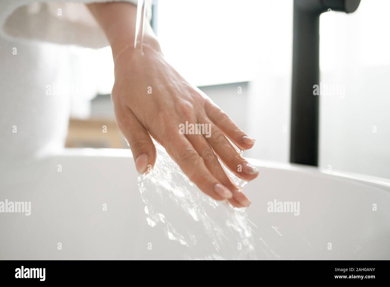 Hand of young woman under pure warm water flowing from tap into bathtub ...