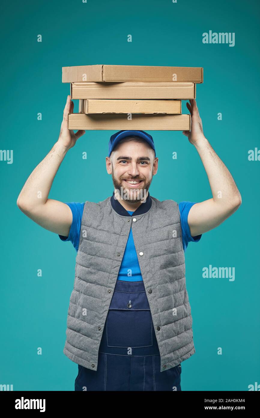 Vertical studio portrait of cheerful food delivery worker holding pizza ...