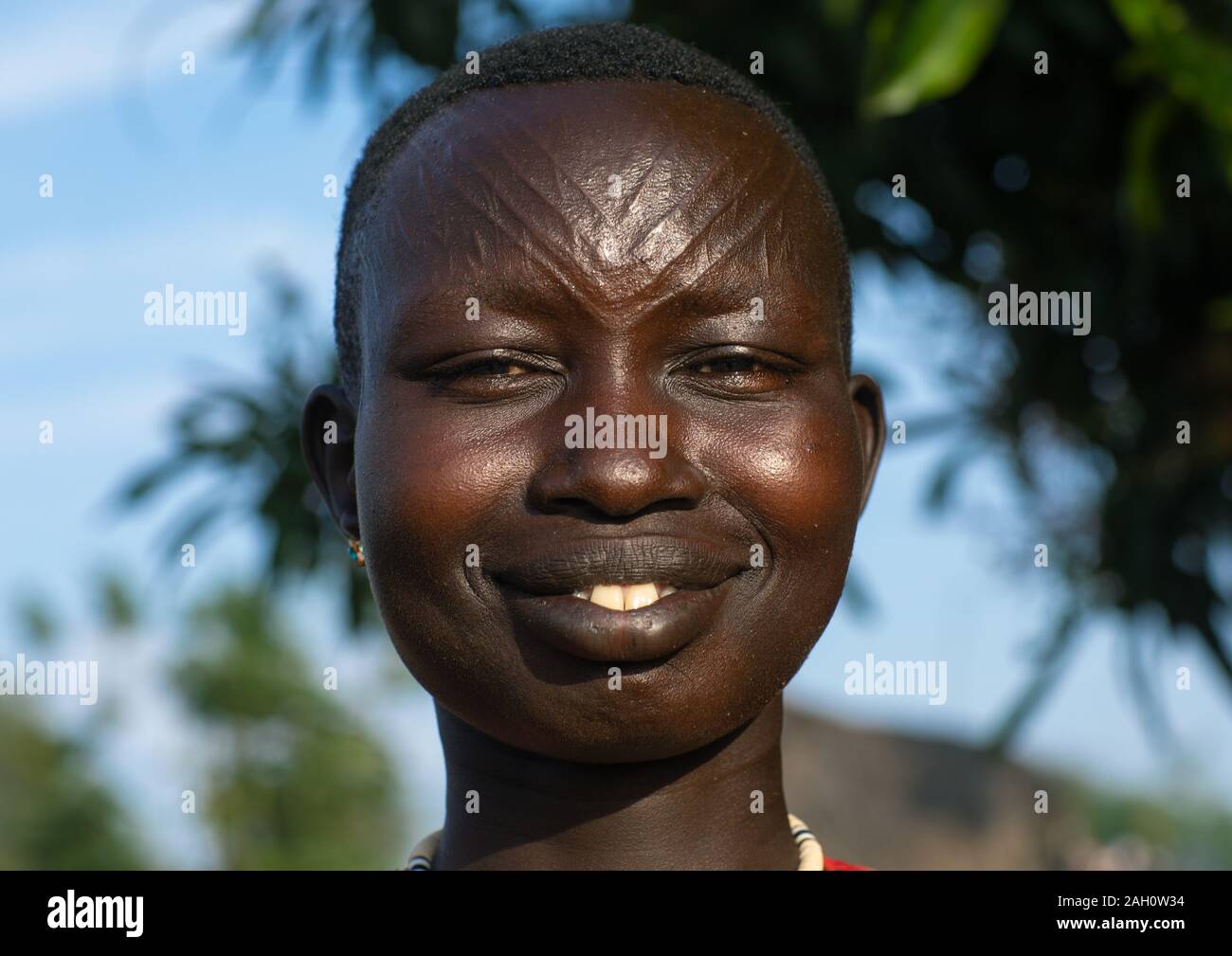 Portrait of a smiling Mundari tribe woman with scarifications on the forehead, Central Equatoria ...
