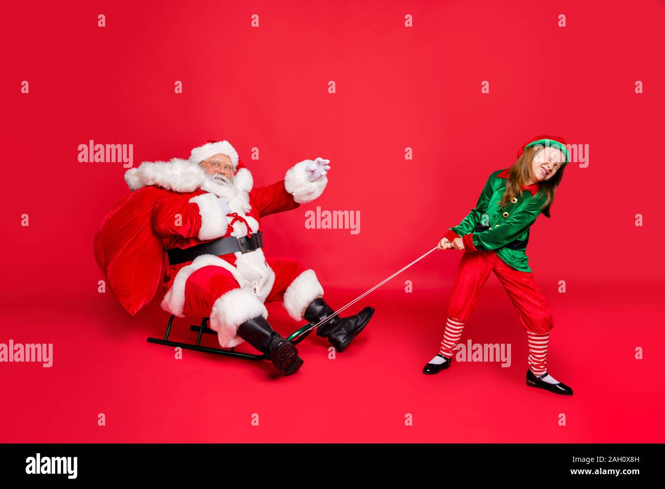 Full body photo of unhappy elf in hat headwear pulling christmas father ...