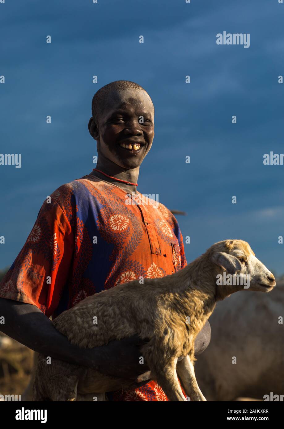 Portrait of a smiling Mundari tribe man carrying a young sheep, Central Equatoria, Terekeka ...