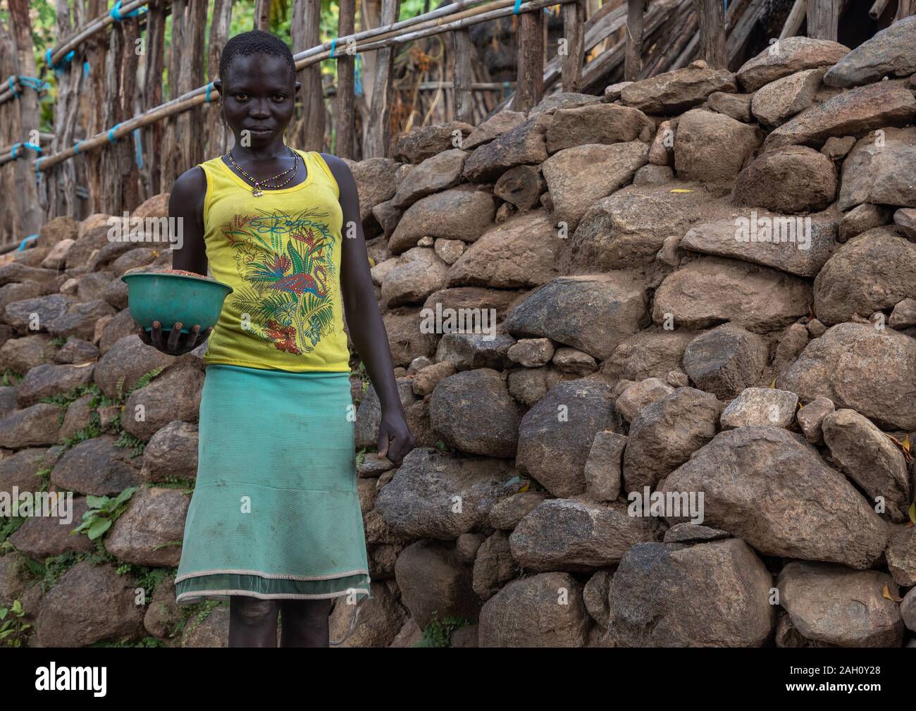 Lotuko tribe woman carrying food in front of a stone wall, Central ...