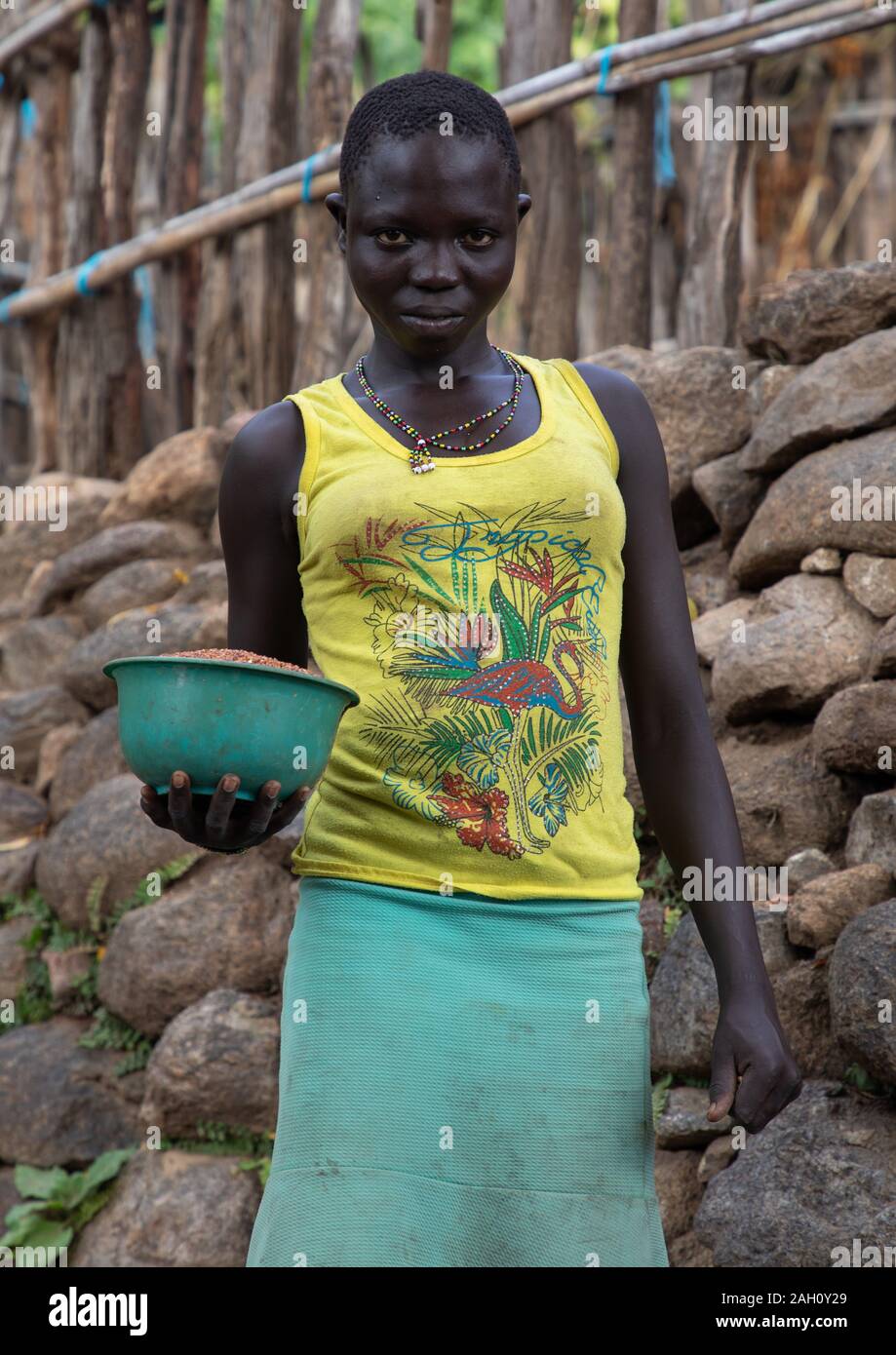 Lotuko tribe woman carrying food in front of a stone wall, Central ...