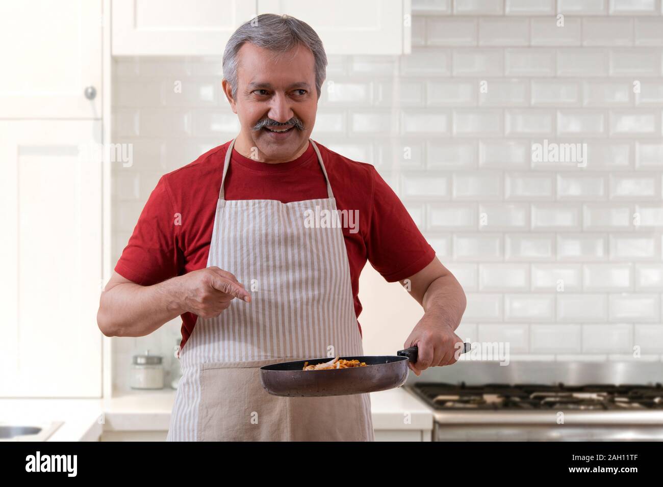 Portrait of a senior man cooking in the kitchen Stock Photo - Alamy