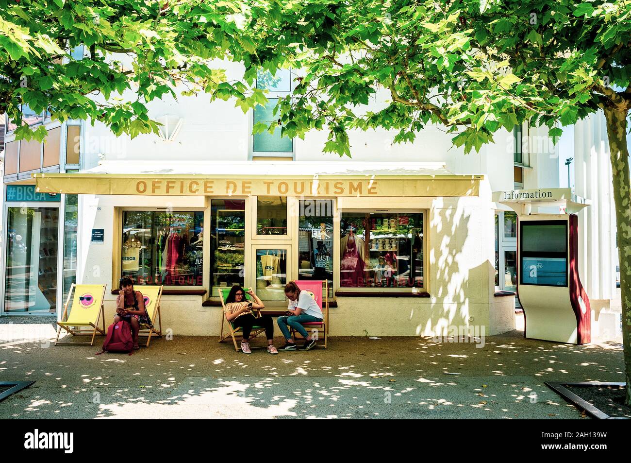 people sitting and relaxing in front of a shop underneath trees on a ...