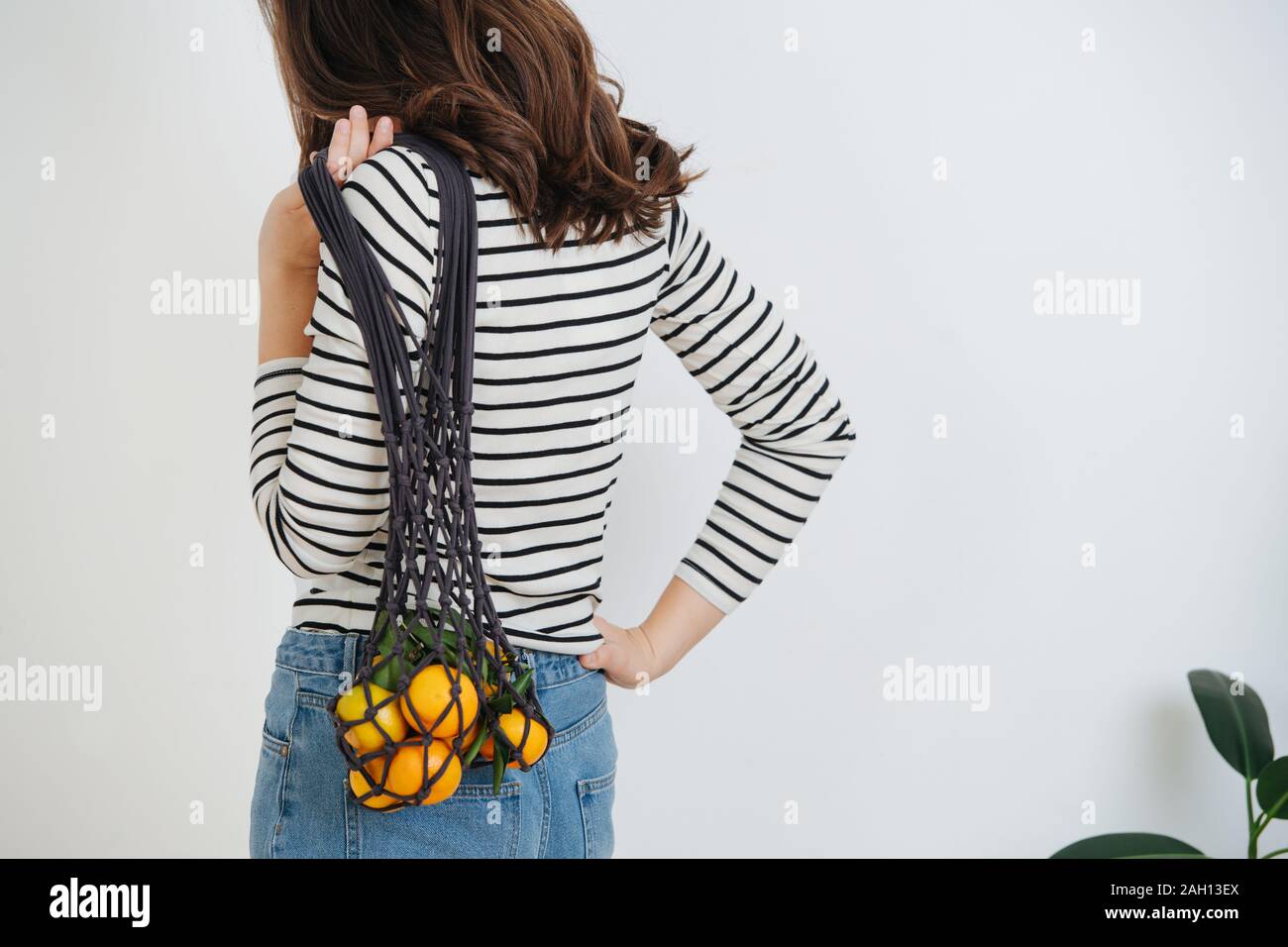 Brunette woman turned her back, posing with a net bag of mandarins over ...