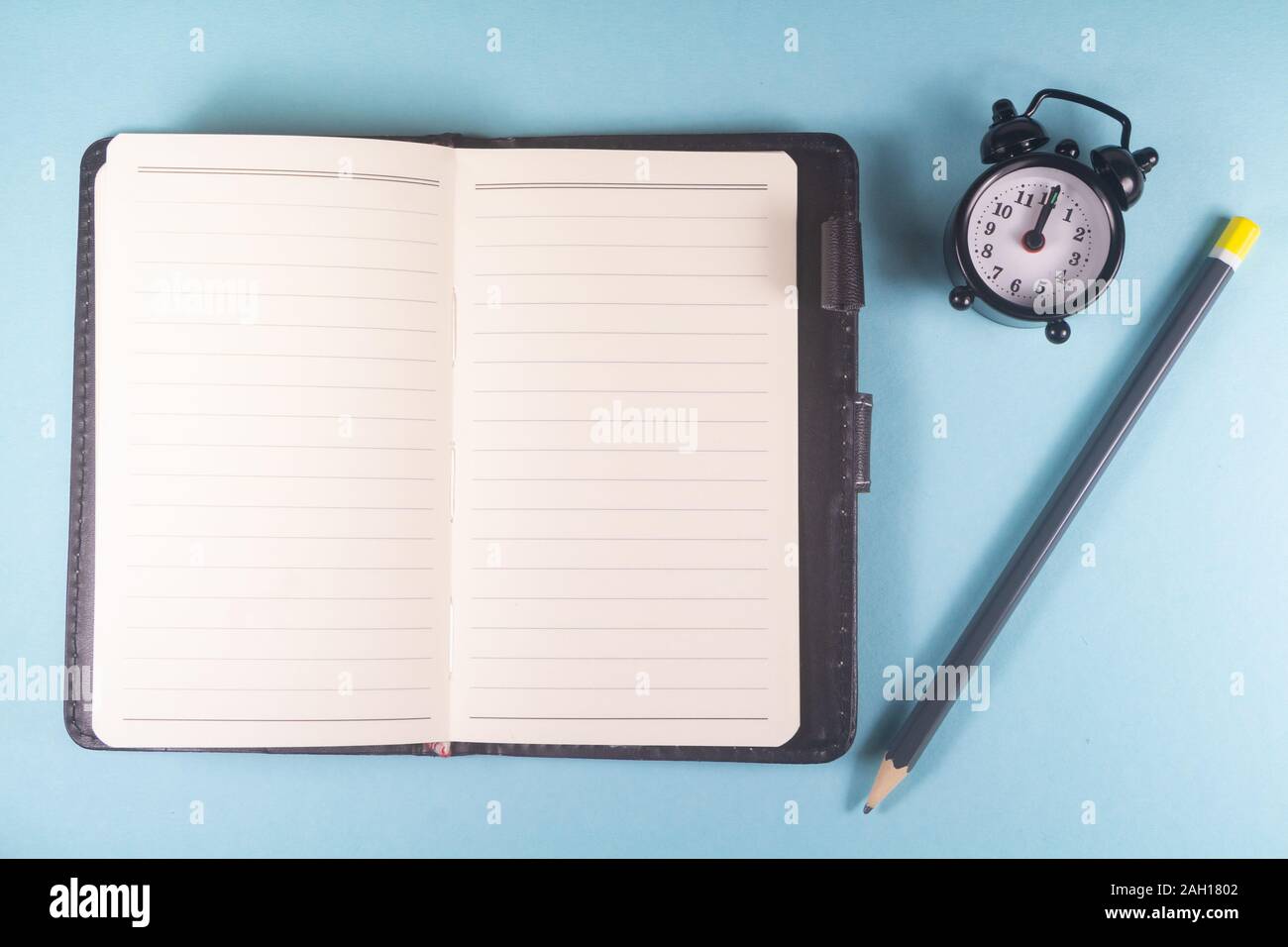 Pencil, open notebook and black alarm clock Stock Photo - Alamy