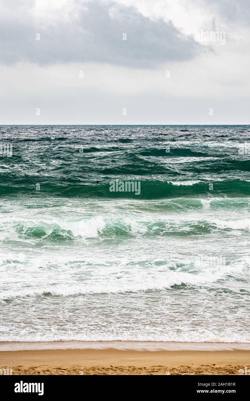 rough sea and waves crashing in to beach and rocks on foreground ...