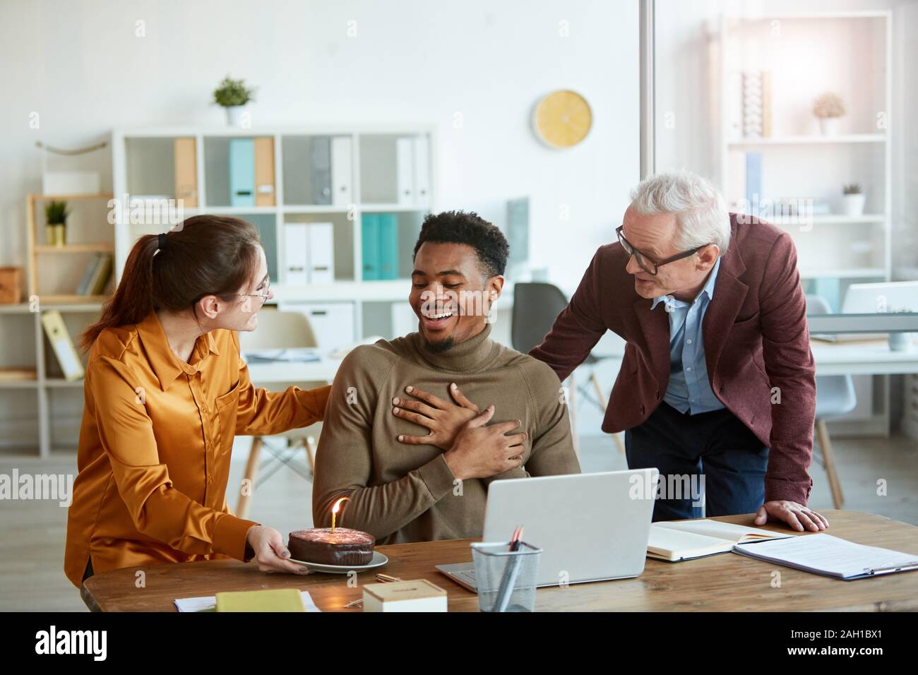 Business people bringing cake with candles for their colleague and they ...