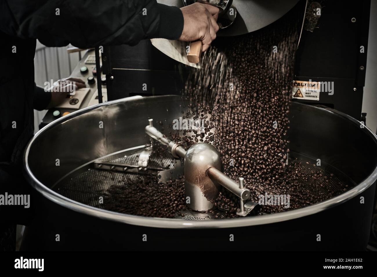 Freshly roasted coffee beans pouring from a large coffee roaster into ...
