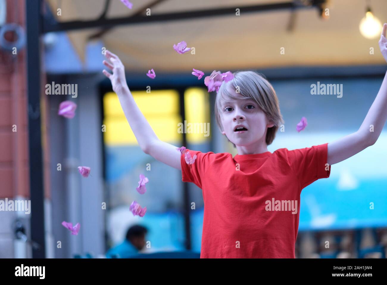 Portrait of a child with arms raised among the falling petals of ...