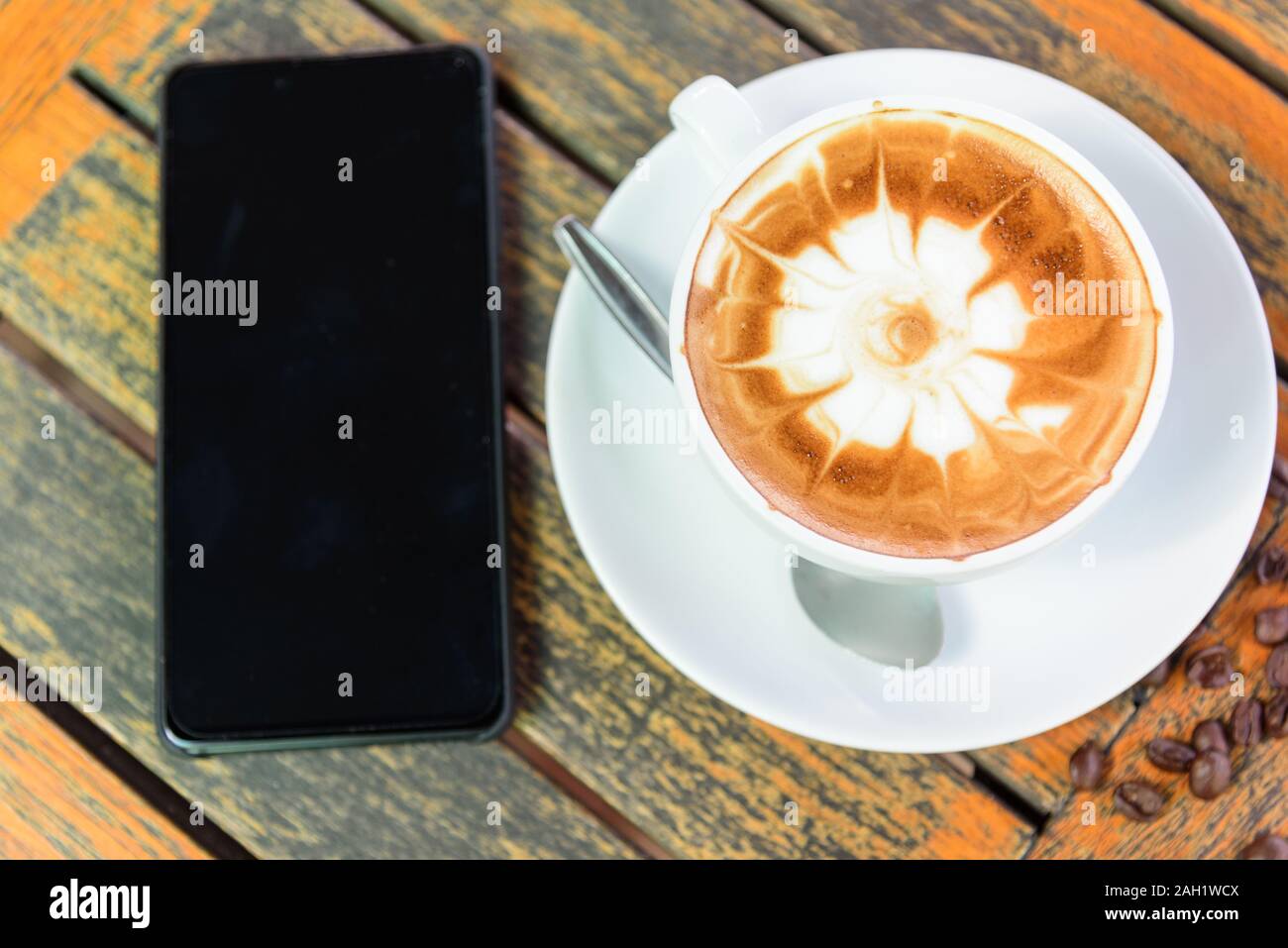 hot cappuccino with nice milk pattern and smart phone on work space ...
