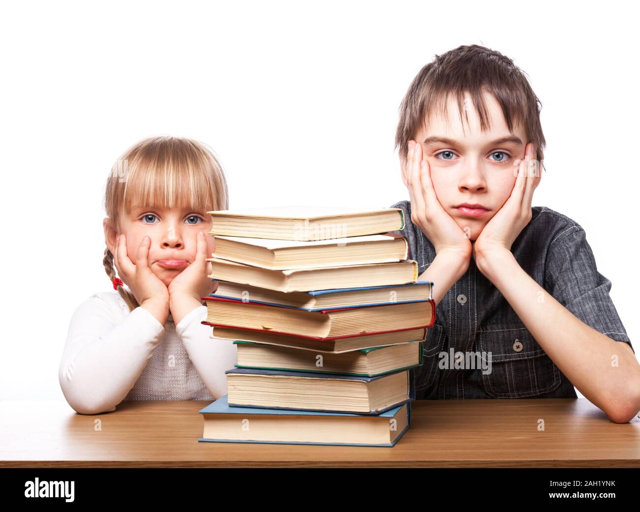 Portrait of frustrated boy and girl sitting at a desk with pile of ...