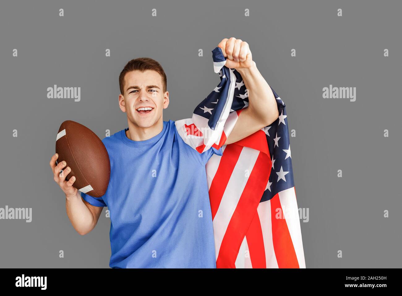 Freestyle. Young man standing isolated on grey with rugby ball and ...