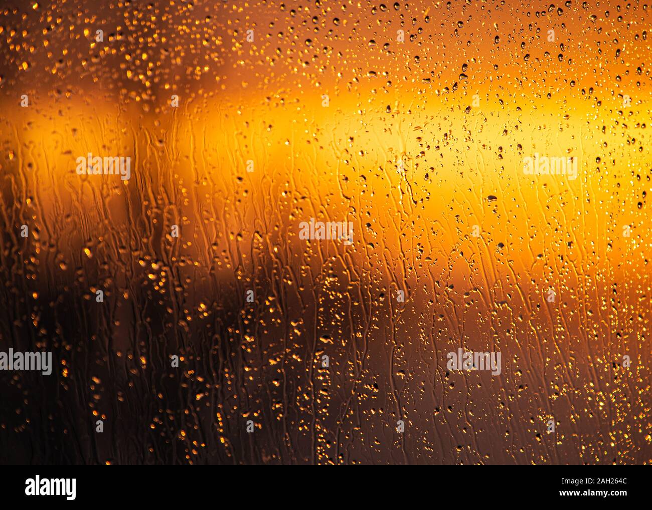 Rain drops on a window during a sunset creating a golden abstract ...