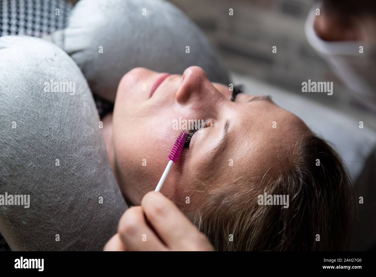 Cosmetologist combs eyelashes of young caucasian woman. Last touches in ...