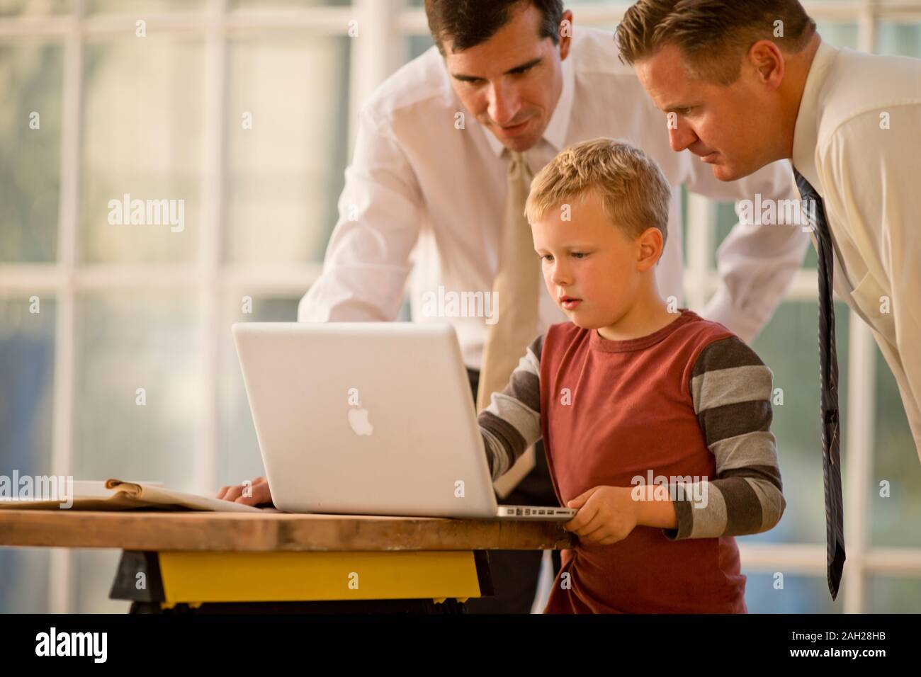 Two businessmen and a young boy looking at a laptop computer Stock ...