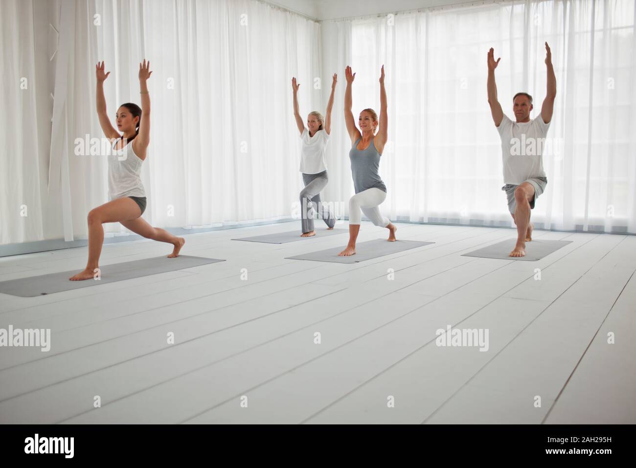 Group of people lunging with arms overhead at a yoga class Stock Photo ...