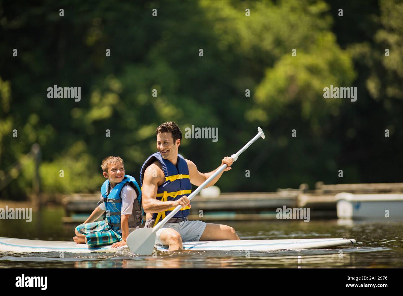 Smiling mid adult man sitting on a paddle board with his son Stock ...