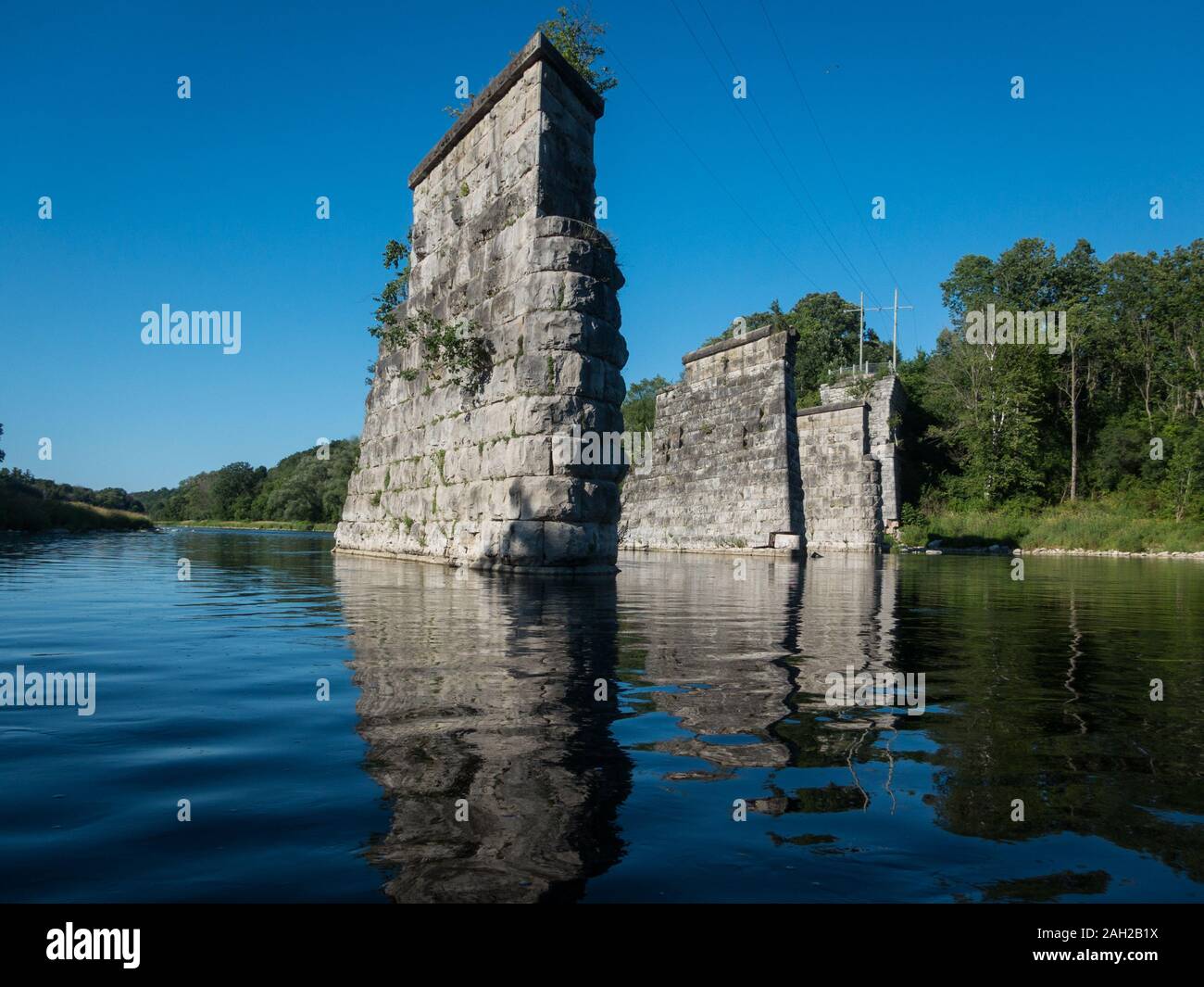 Abandoned and crumbled bridge pillar shot from river with reflections ...
