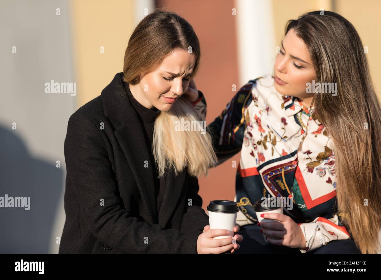 Young woman cheering up crying female friend at the street with ...
