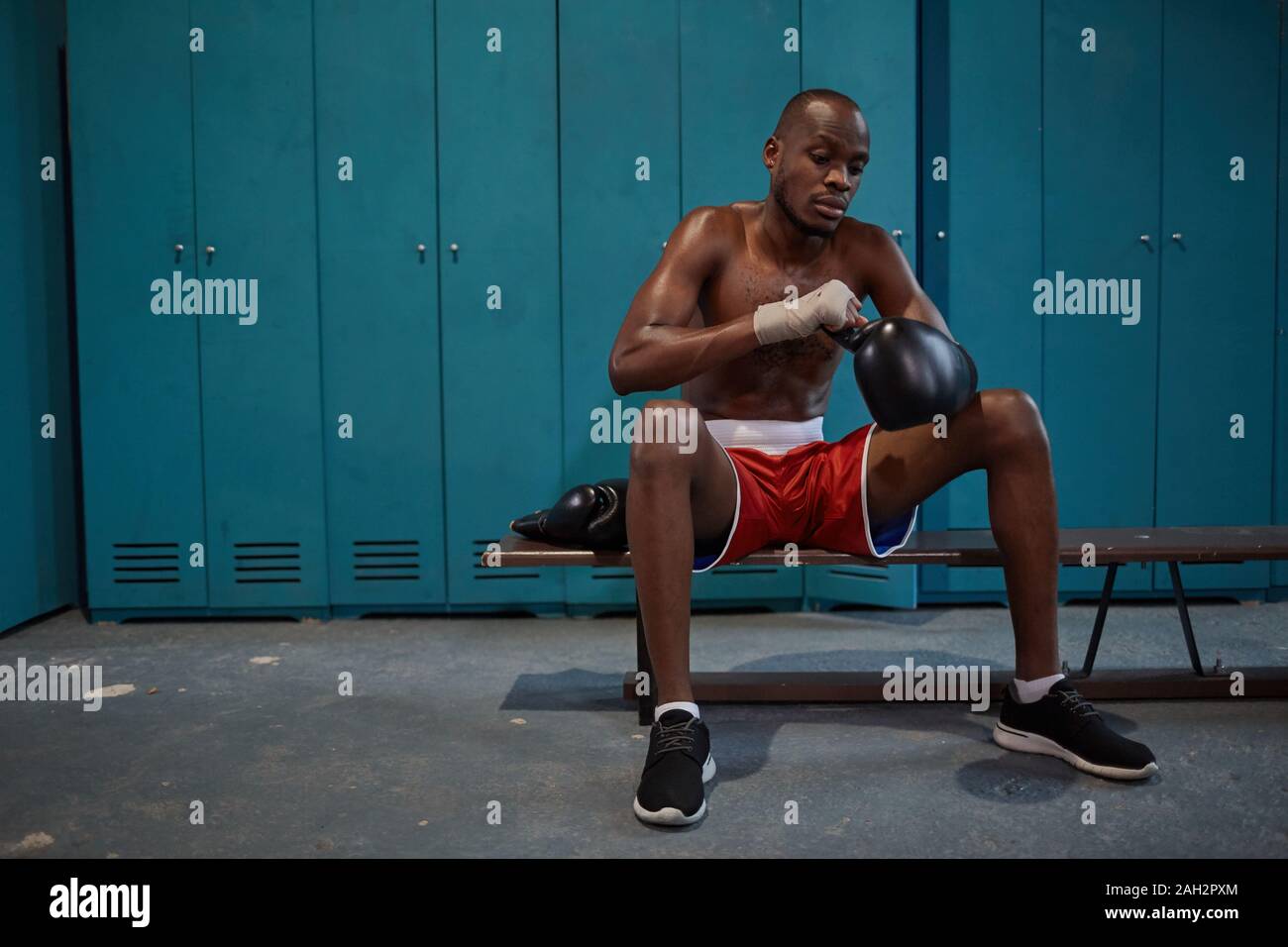 Serious African young boxer wearing boxing gloves while sitting on ...