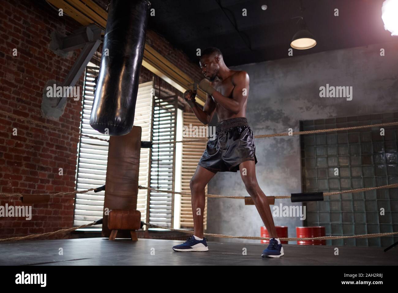 African muscular boxer fighting with punching bag on boxing ring in the ...