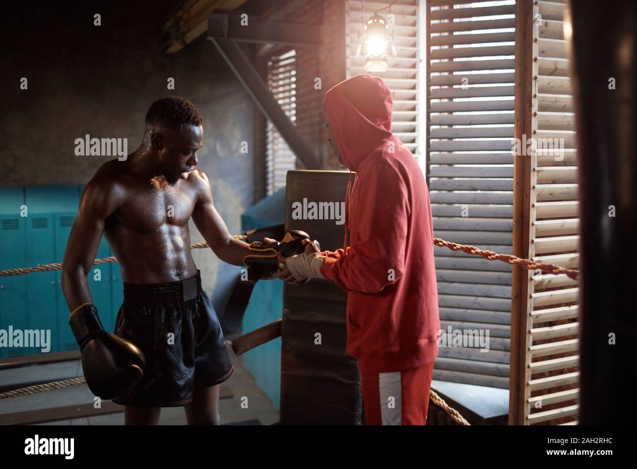African muscular sportsman standing on boxing ring while his coach ...
