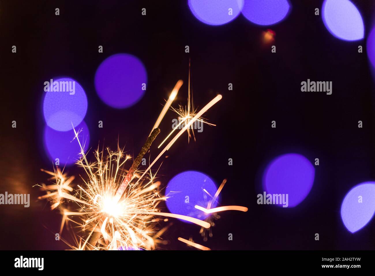 Lit sparkler on the background of flickering garlands Stock Photo - Alamy