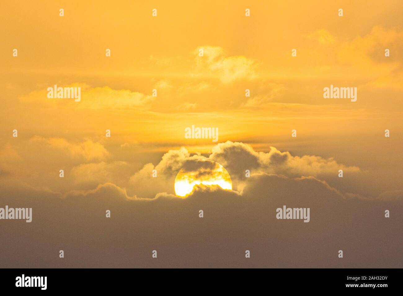 The sun rising above clouds with a yellow sky and the sun partially ...