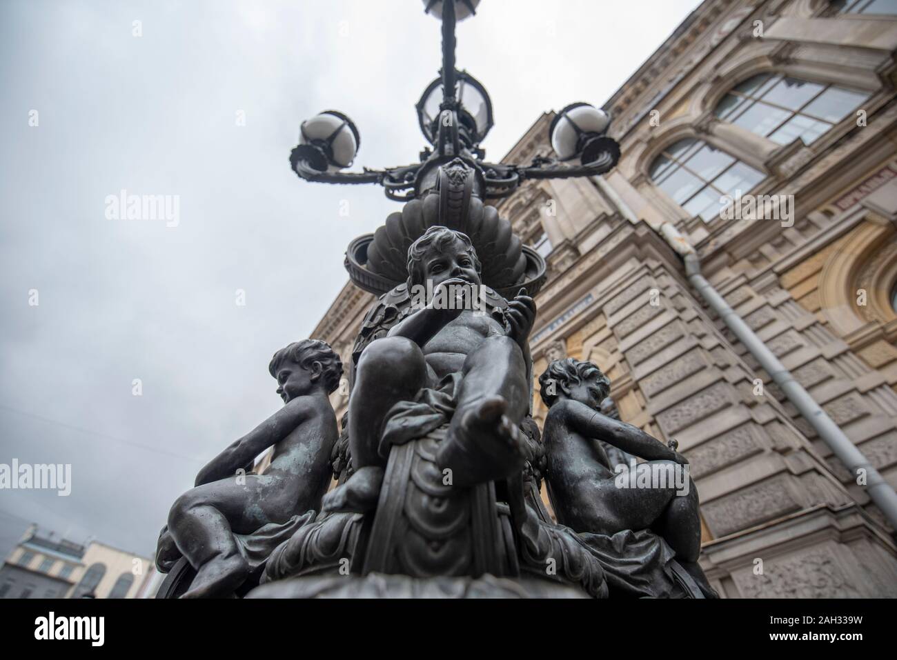 Bronze angel boy statue with a human figure in hands. Part of street lantern composition in ...
