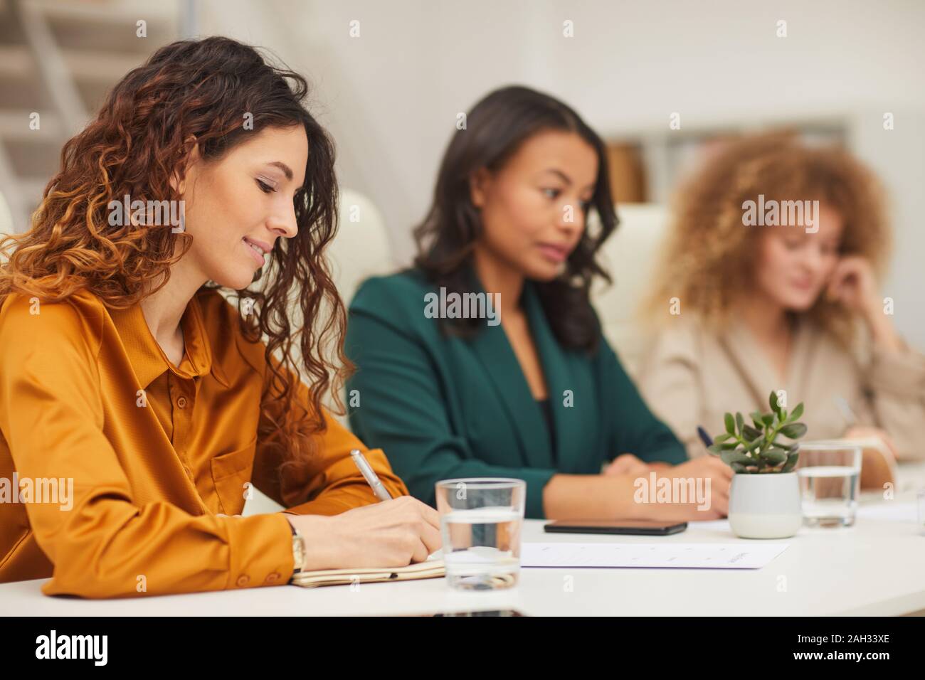 Horizontal eye level shot of three stylish young women making notes ...
