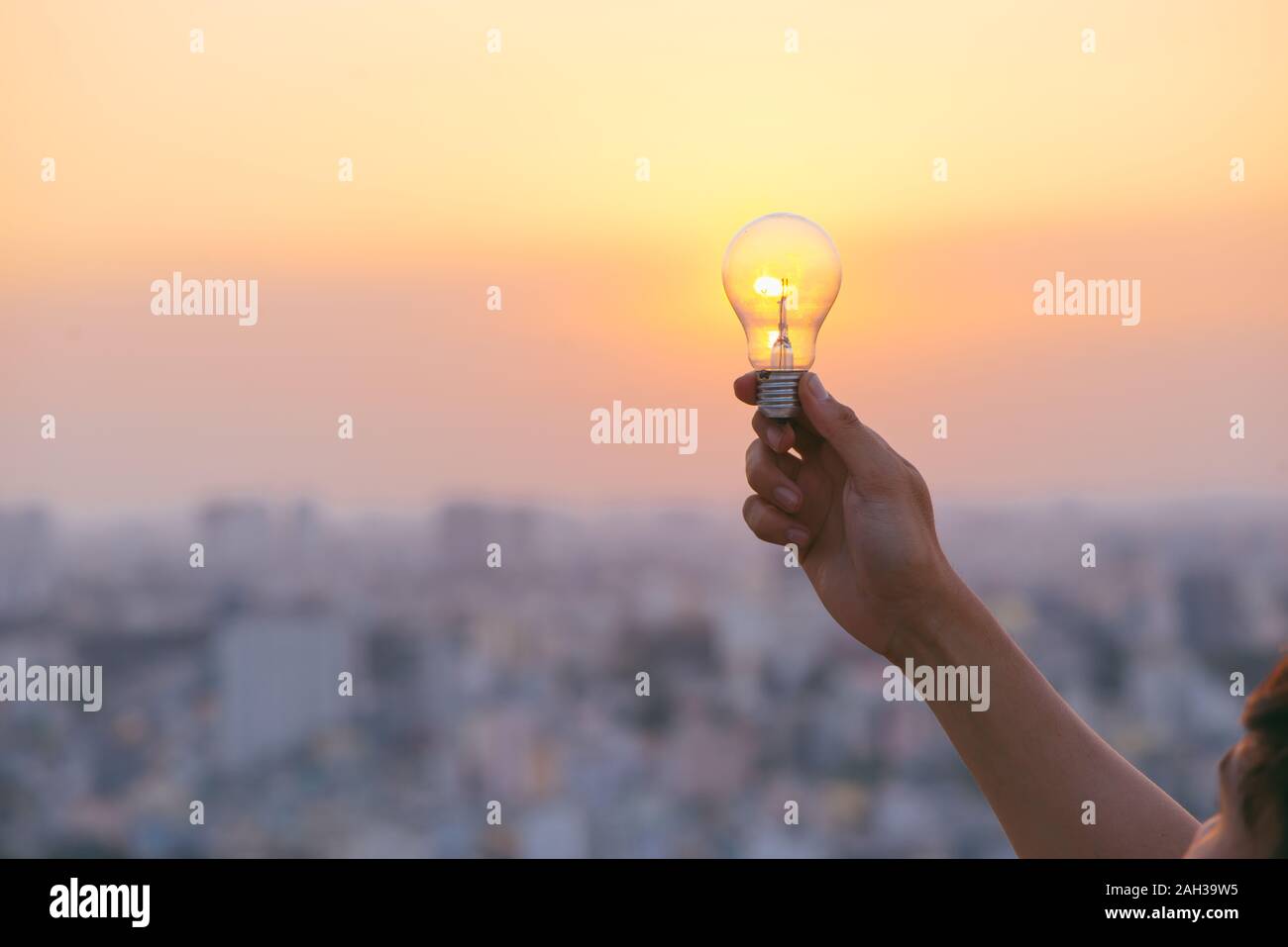 Hand hold a light bulb on sunset background for saving energy and ...