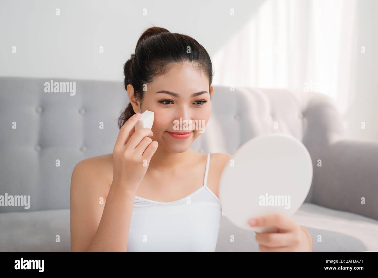 Beautiful asian woman using cosmetic sponge on face and look mirror at ...